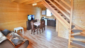 Interior de uma cabana de madeira com área de refeições, cozinha e escada.
