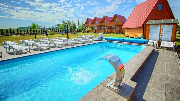 Piscina com espreguiçadeiras, toboágua e um edifício com telhado vermelho ao fundo.