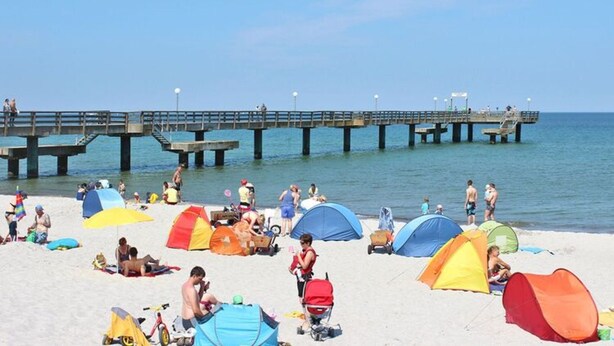 Uma praia com várias tendas coloridas e um cais ao fundo.