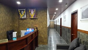 Uma área de recepção de hotel com balcão, sala de espera com sofá e corredor que leva a uma escadaria.