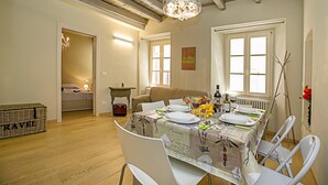 Uma sala de jantar com uma mesa posta para quatro pessoas, um candelabro e vista para um quarto por uma porta aberta.