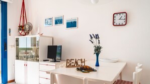 Quarto compacto com uma mesa branca, um pequeno escritório com um computador, um relógio e quadros nas paredes.