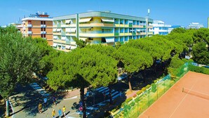 Um edifício com vários andares e varandas, cercado por árvores e uma quadra de tênis.