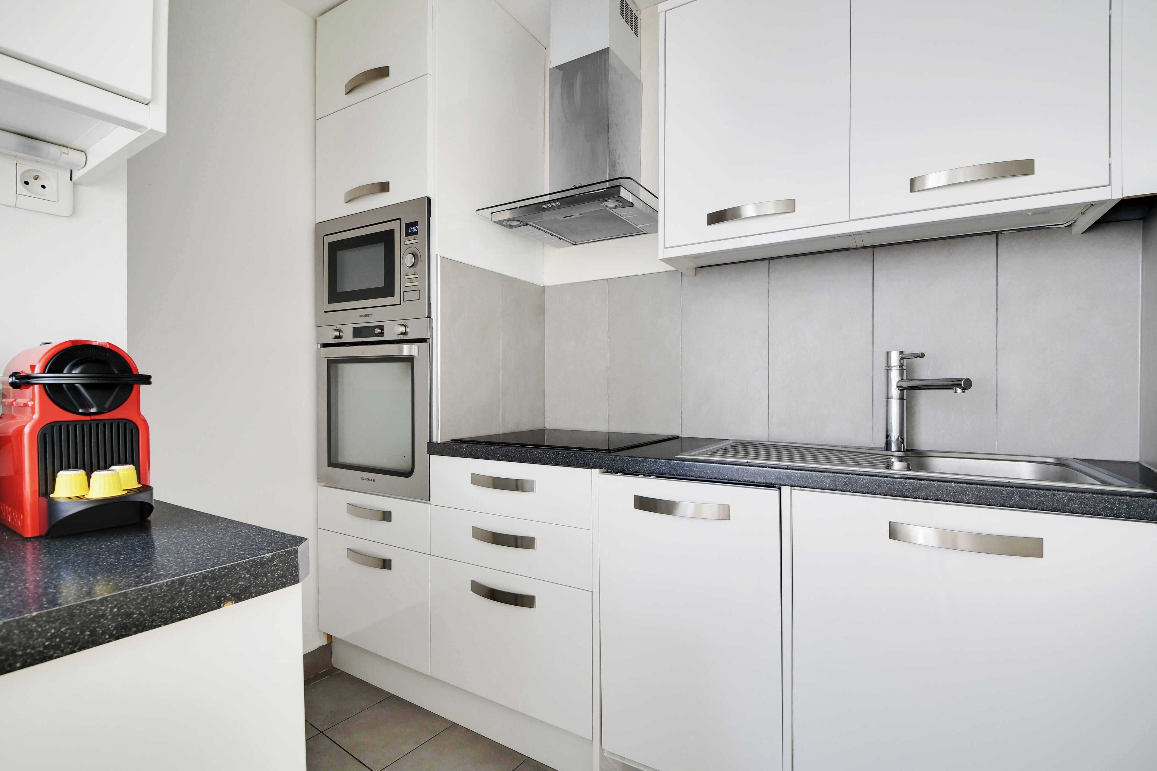 Cozinha moderna com armários brancos, bancada preta, eletrodomésticos de aço inoxidável e um eletrodoméstico vermelho na bancada.