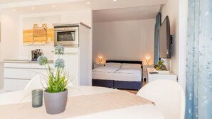 Quarto de hotel moderno com cama, mesa de cabeceira, luminária e uma área de cozinha compacta com fogão e forno.