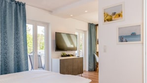 Quarto com cama, televisão em um móvel e varanda com cortinas.