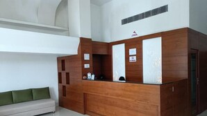 Um balcão de recepção com acabamento em madeira, um sofá verde e um chão de azulejos brancos.