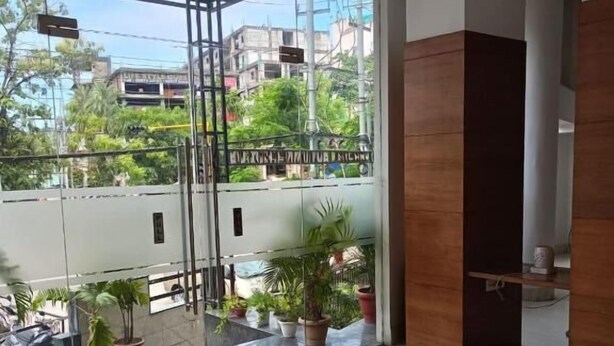 Amplo espaço interno com porta de vidro que dá para uma varanda, plantas em vasos e piso ladrilhado.
