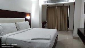 Quarto de hotel com uma cama grande, cabeceira, televisão de tela plana e porta de correr para uma varanda.