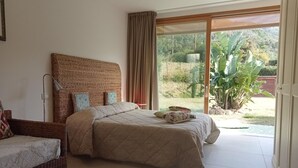 Quarto com cama, uma cadeira de vime e vista para o exterior.