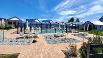 Área de piscina com estrutura de vidro, espreguiçadeiras e um pátio de tijolos.
