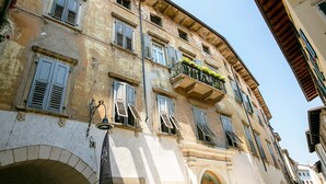Um edifício histórico com várias janelas, algumas com persianas, e uma varanda com plantas.