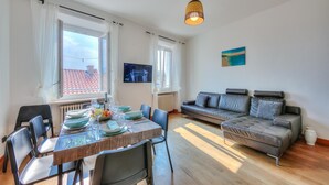 Uma sala de estar moderna com área de jantar, um sofá cinzento e uma televisão na parede.