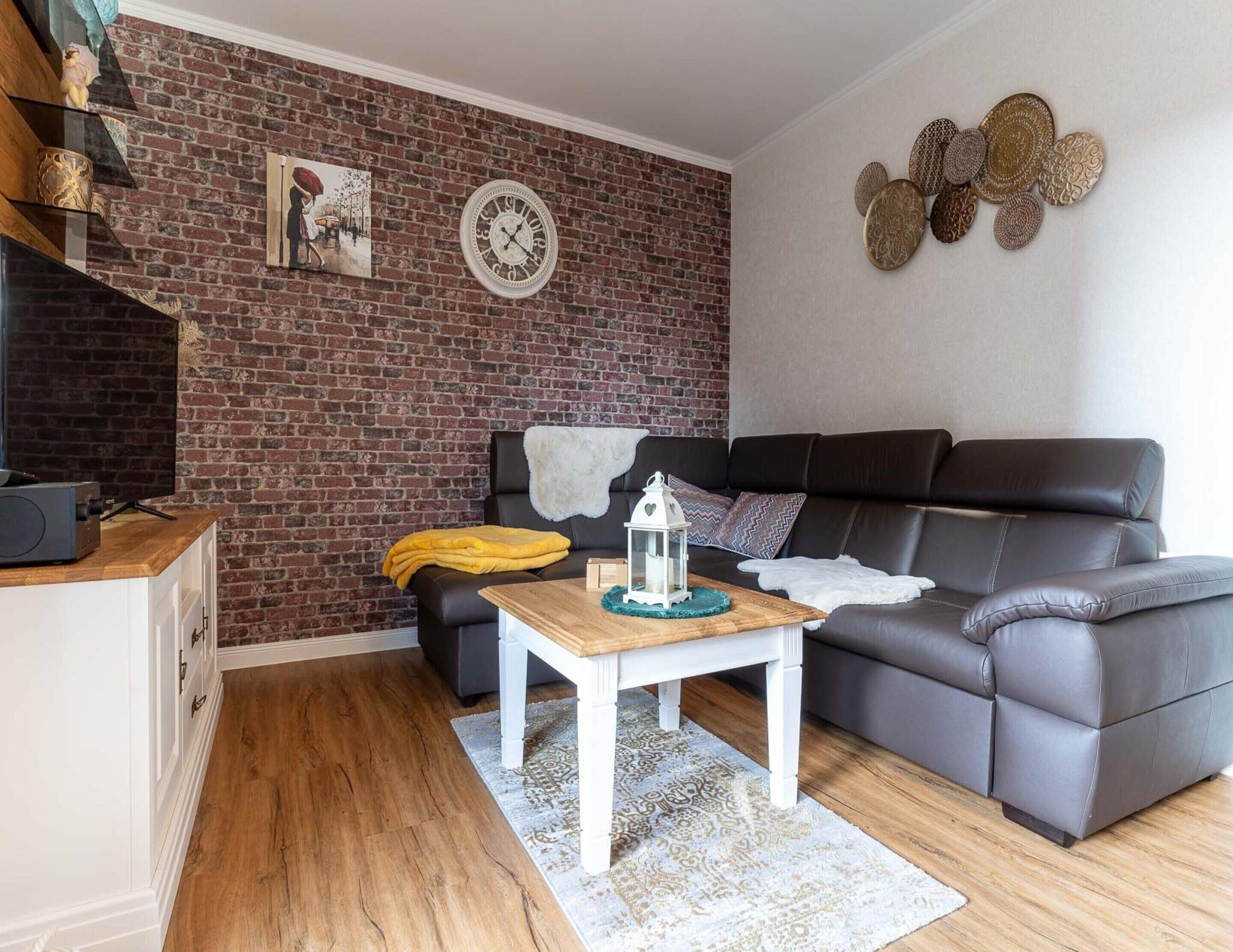 Uma sala de estar com parede de tijolos, um sofá cinzento, uma mesa branca e um armário de madeira.