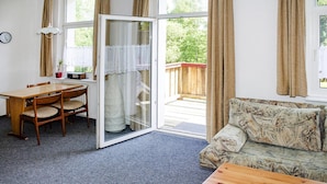 Um quarto com uma mesa de jantar e cadeiras de madeira, um sofá, uma mesa de centro de madeira e uma porta de vidro deslizante que dá para um deck externo.