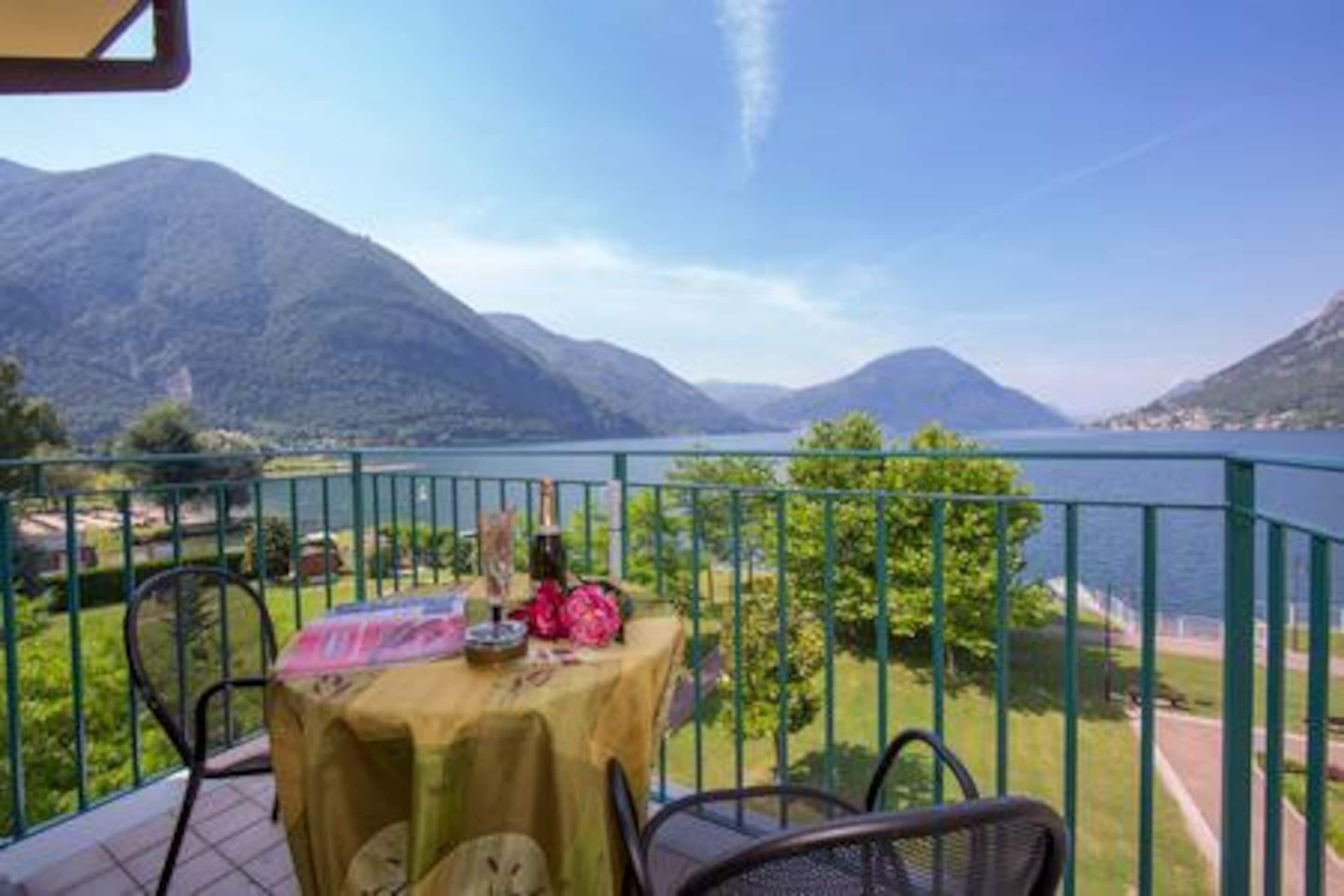 Varanda com mesa posta para refeições, com vista para um lago e montanhas.