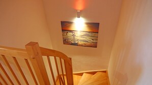 Uma escada de madeira com um quadro de um pôr do sol sobre o oceano na parede.