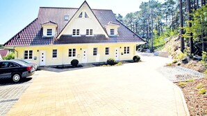 Um edifício de dois andares com telhado de telhas, calçada e área de estacionamento com dois carros.
