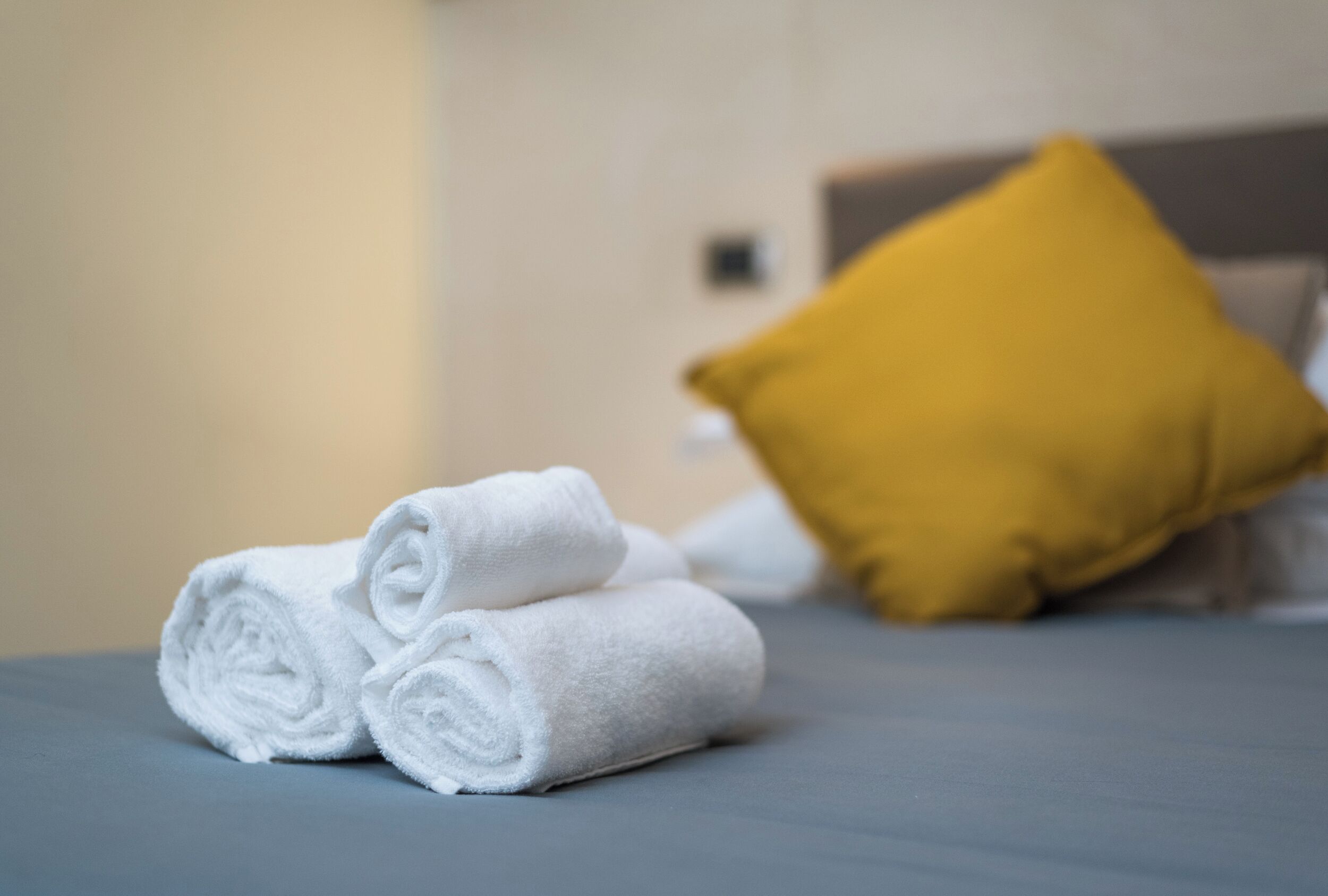 Cama bem arrumada com toalhas brancas dobradas e um único travesseiro amarelo.