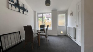Um quarto com uma mesa de jantar e cadeiras, um radiador, uma porta e uma janela.
