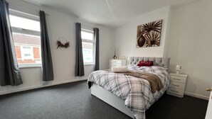 Quarto com cama, mesa de cabeceira, obra de arte na parede e janela com cortinas.