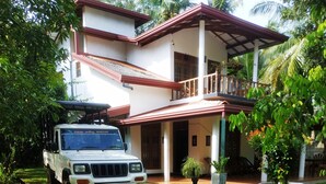 Uma caminhonete branca estacionada em um caminho de acesso pavimentado que leva a uma casa de dois andares com telhado vermelho e paredes brancas.