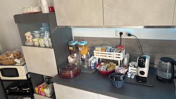 Uma cozinha com máquina de café, micro-ondas e diversos alimentos sobre o balcão.