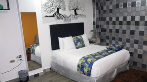 Quarto com cama, mesa de cabeceira, espelho e parede com desenho de árvore e cabeça humana.