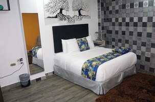 Quarto com cama, mesa de cabeceira, espelho e parede com desenho de árvore e cabeça humana.