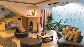 Um hall de hotel moderno com escada, sofás de couro preto, uma mesa de centro e plantas em vasos.