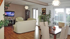 Uma sala de estar com sofá, mesa de jantar, cadeiras, televisão e um quadro.