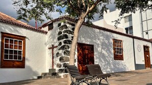 Um edifício com parede de pedra, porta de madeira e duas bancas em frente.