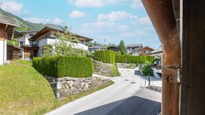 Uma rua residencial com casas, um muro de pedra e céu claro.