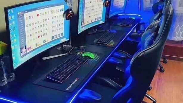 Configuração de computador com vários monitores, teclado e rato em uma mesa.