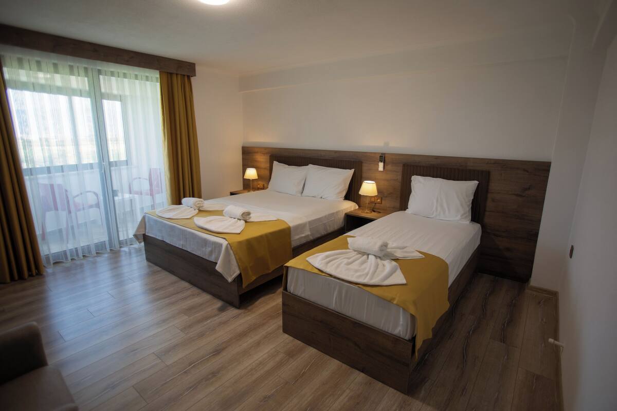 Quarto de hotel com duas camas, piso de madeira e varanda com cortinas.