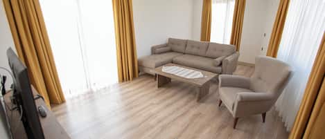 Uma sala de estar moderna com um sofá de canto, uma poltrona, uma mesa de centro e uma TV de tela plana.