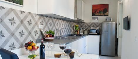 Uma cozinha moderna com área de jantar, com uma mesa branca posta para dois, uma geladeira, um micro-ondas e uma pia.