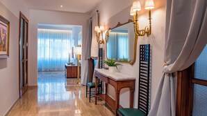 Corredor de hotel com piso de mármore, mesa de console de madeira, espelho e planta em vaso.