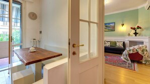 Um quarto com uma mesa de madeira, uma porta com puxador de latão, um relógio na parede, um sofá com capa floral e uma lareira.