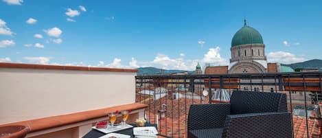 Terraço com mesa posta para dois, com vista para um edifício histórico com cúpula verde.