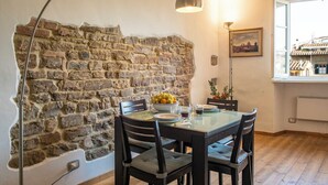 Uma sala de jantar com uma parede de pedra, uma mesa posta com pratos, copos e uma tigela de frutas.