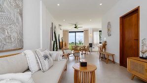 Uma sala de estar moderna com um sofá, mesa de madeira redonda e uma área de refeições com cadeiras.