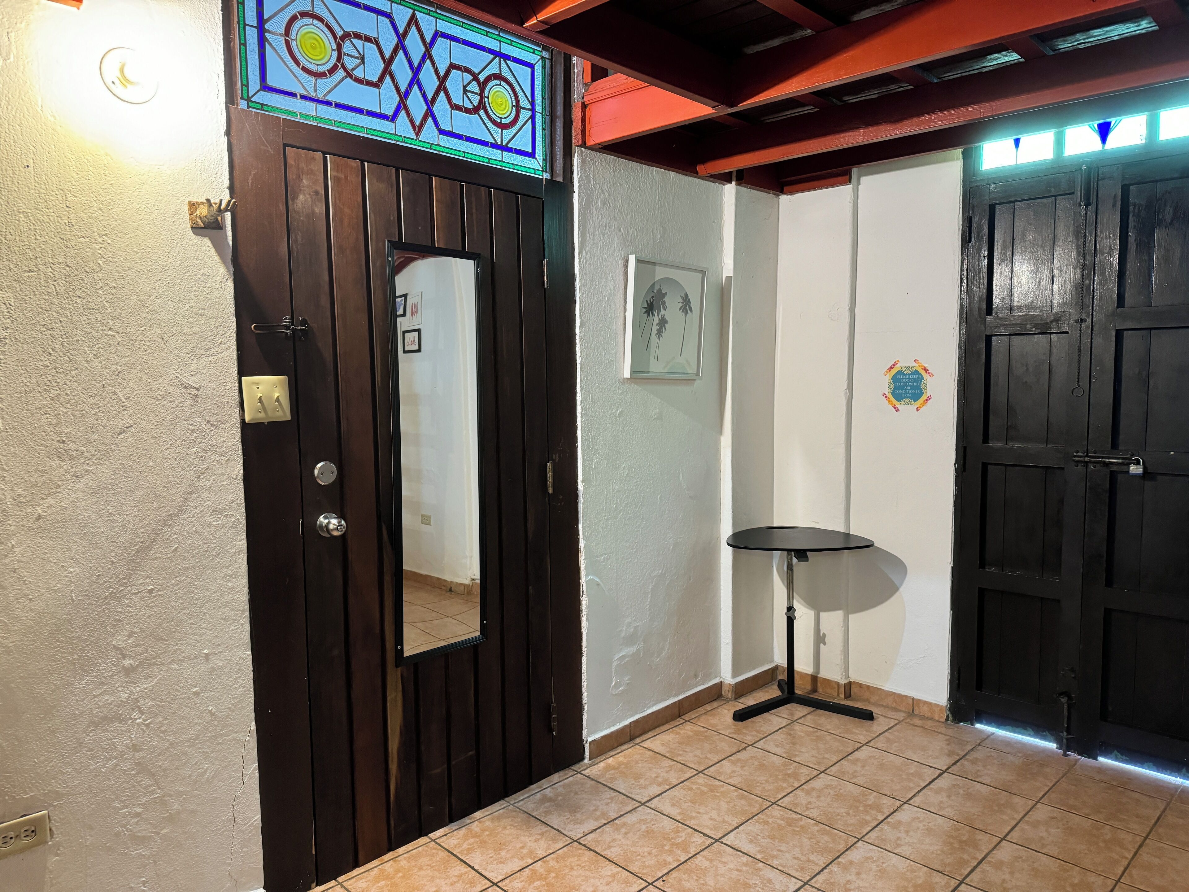 Um corredor com uma porta de madeira, uma mesa redonda pequena e chão de azulejos.