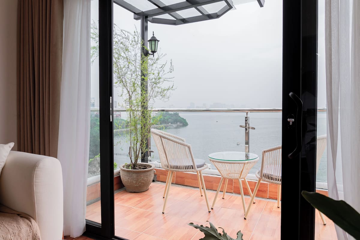 Uma varanda com vista para a água, cadeiras de vime, uma mesa de vidro e um vaso com planta.