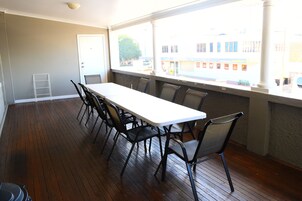 Sala de conferências com uma mesa comprida e cadeiras, janelas amplas com vista para edifícios.