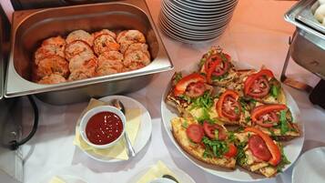 Uma mesa de buffet com diversos pratos, incluindo carne fatiada, sanduíches de frango grelhado e uma tigela de molho vermelho.