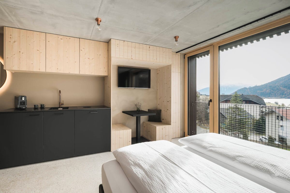 Quarto moderno com cama grande, escrivaninha embutida, televisão e varanda com vista para as montanhas.