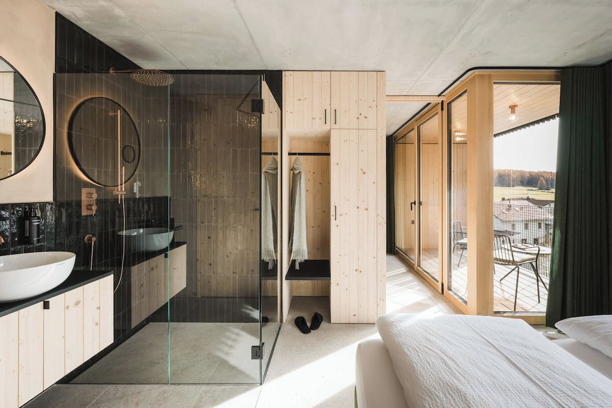 Quarto moderno com uma cama grande, banheiro com box de vidro e vista da cidade através de amplas janelas.