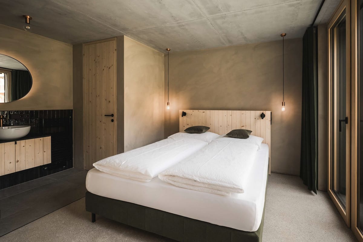 Quarto moderno com cama grande, cabeceira de madeira, espelho redondo e pia embutida.