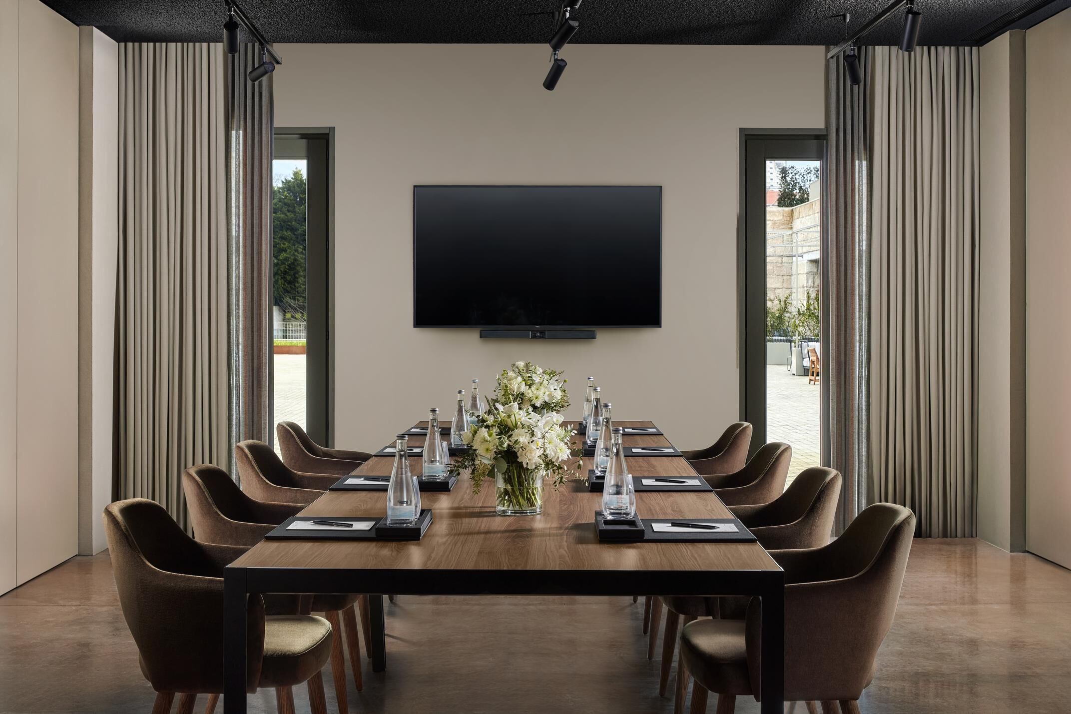 Uma sala de conferências com uma mesa comprida, cadeiras, uma televisão e um vaso de flores.